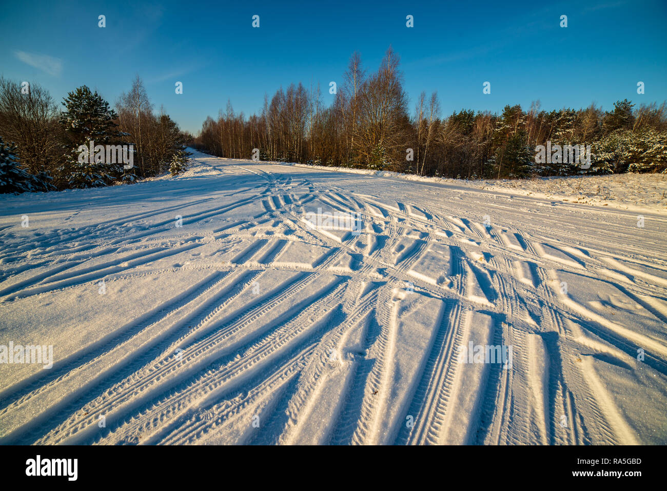 snow covered winter road with tire tracks in perspective with blue sky ...