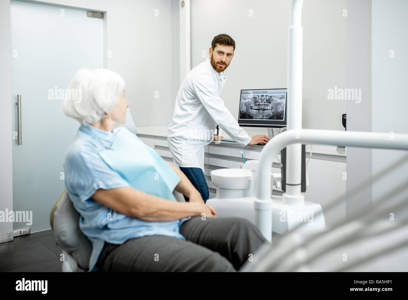 Dentist showing panoramic shot of the jaw on the computer to the elder ...