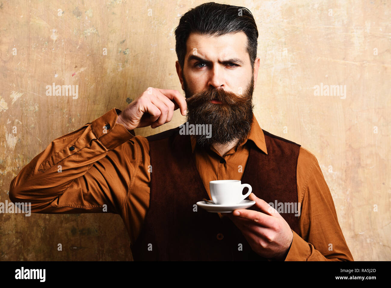Young male waiter in uniform holding cup of coffee over beige texture ...