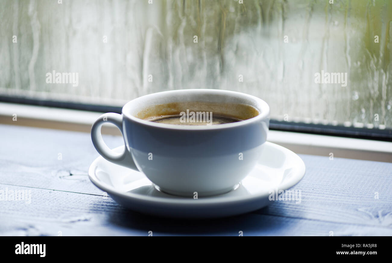 Wet glass window and cup of hot coffee. Autumn cloudy weather better ...