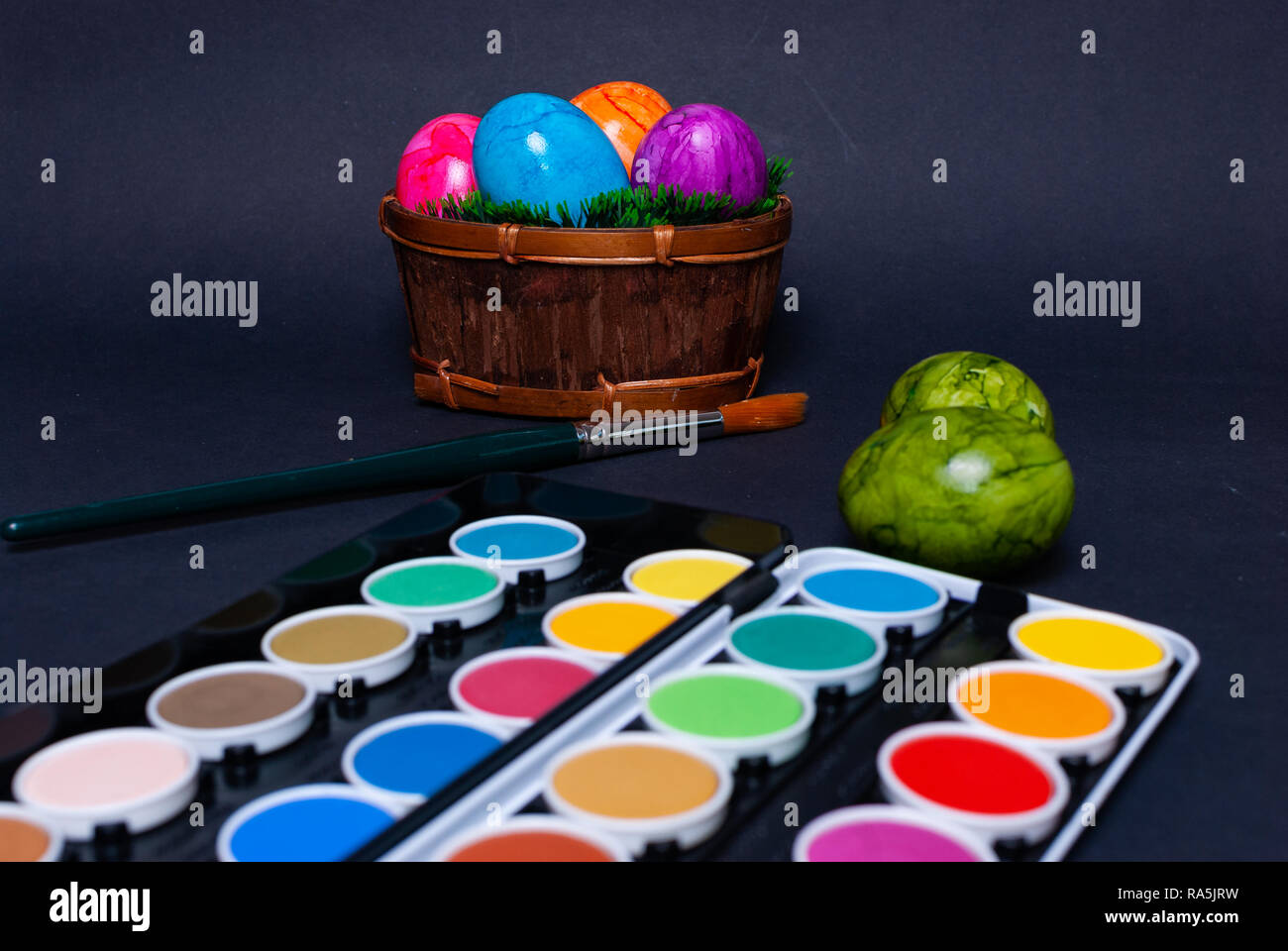 Colorful easter eggs in a basket a pallet of colors and a paintbrush on ...