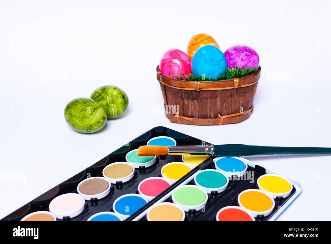 Colorful easter eggs in a basket a pallet of colors and a paintbrush on ...