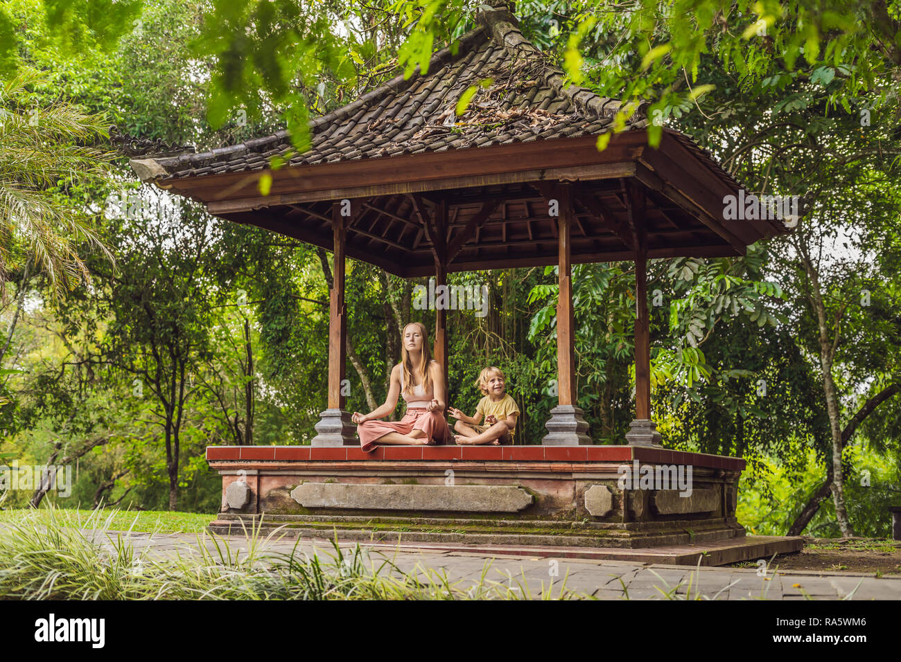 Mom and son meditate practicing yoga in the traditional balinesse ...