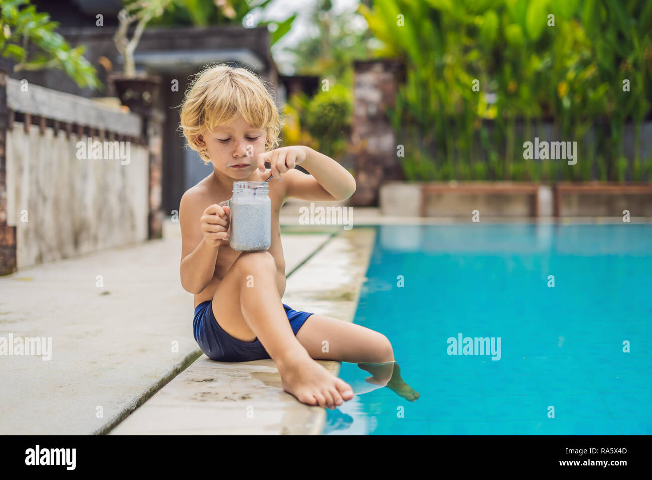 The boy eats chia pudding in the morning by the pool. Healthy breakfast ...