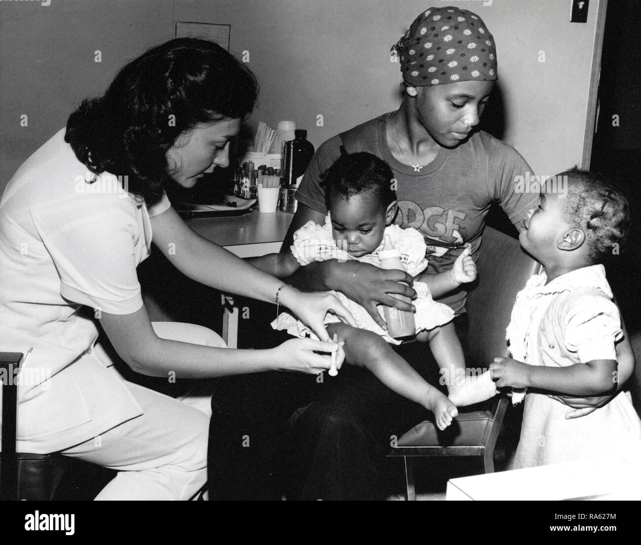 an African American child receives an injection in her leg just above ...