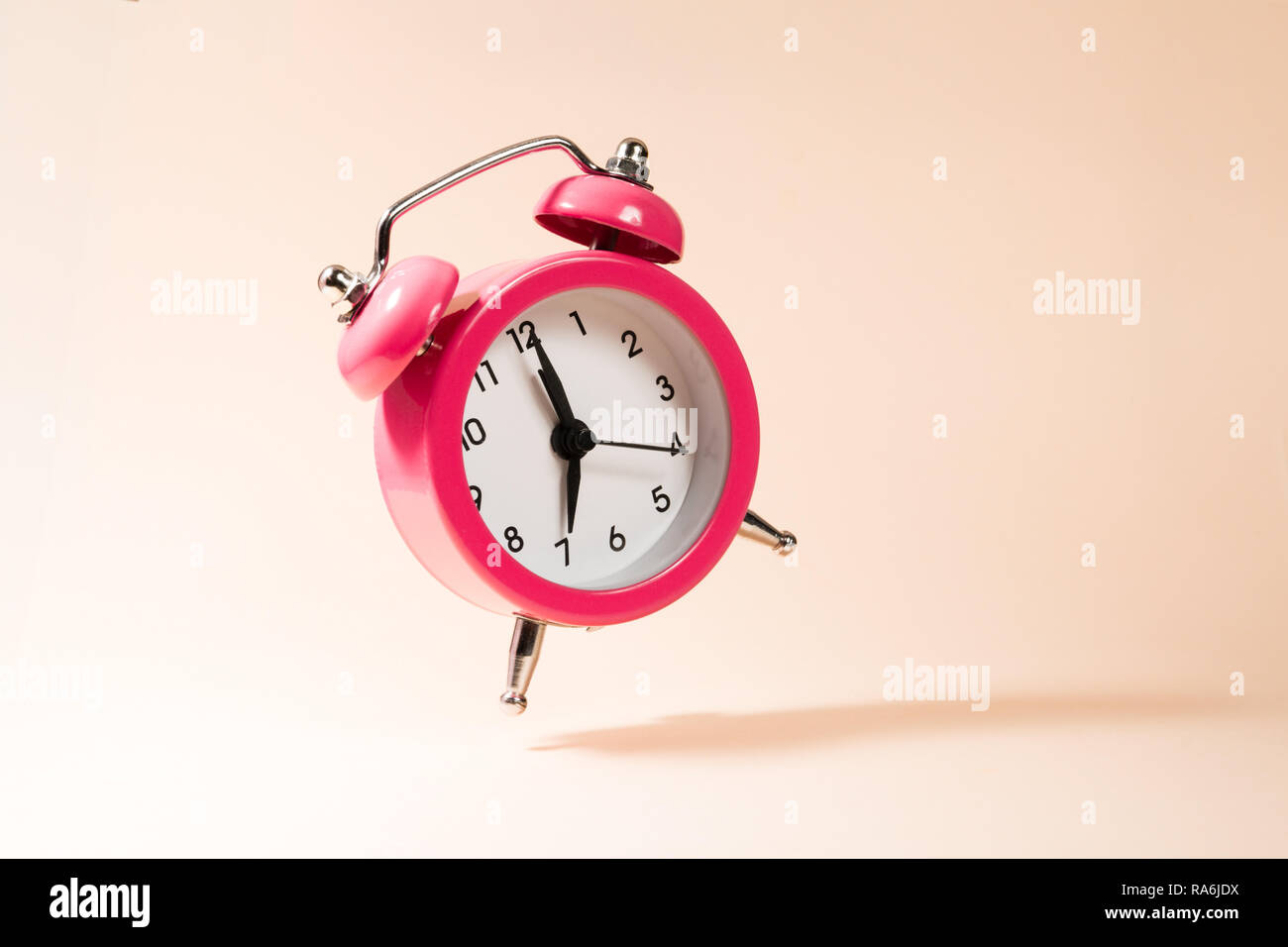 The morning alarm clock jumping up from the bell on a peach background ...