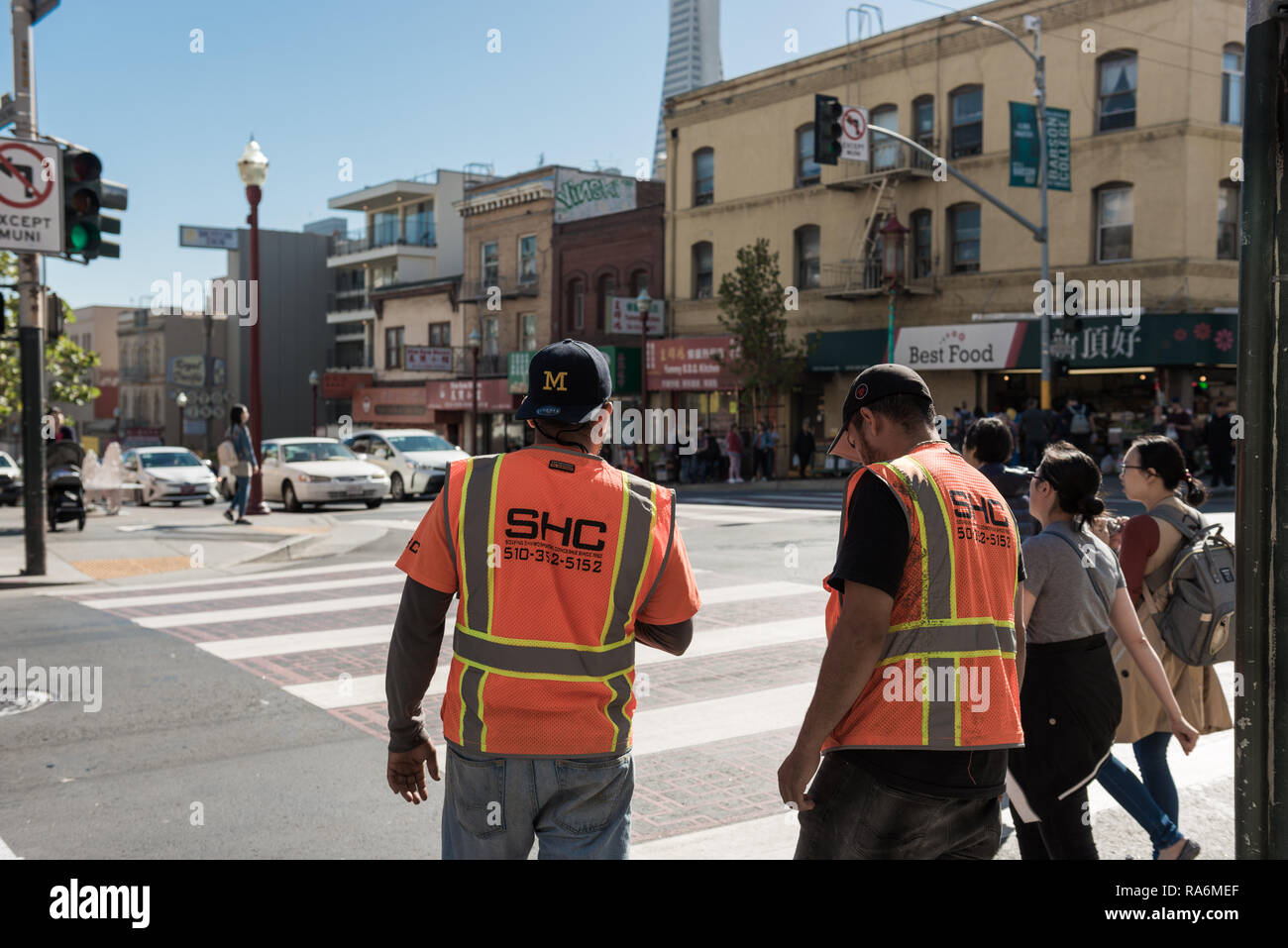 Workers with orange vests wait to cross a street in San Francisco ...