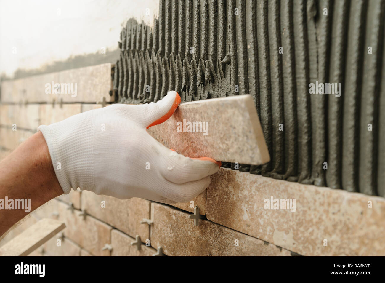 Installing the tiles on the wall. A worker putting tiles in the form of ...