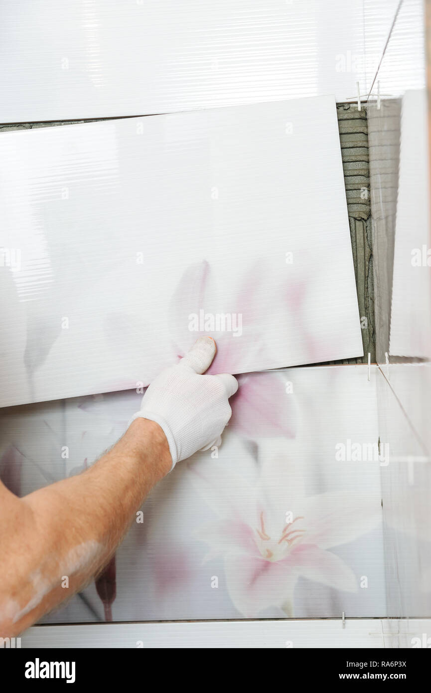 Installing the tiles on the wall. A worker putting tiles in the ...