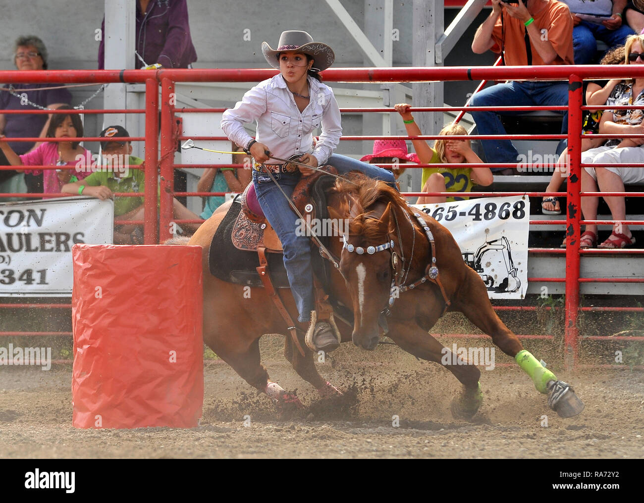 A young barrel racer guides her horse around a barrel at high speed in ...