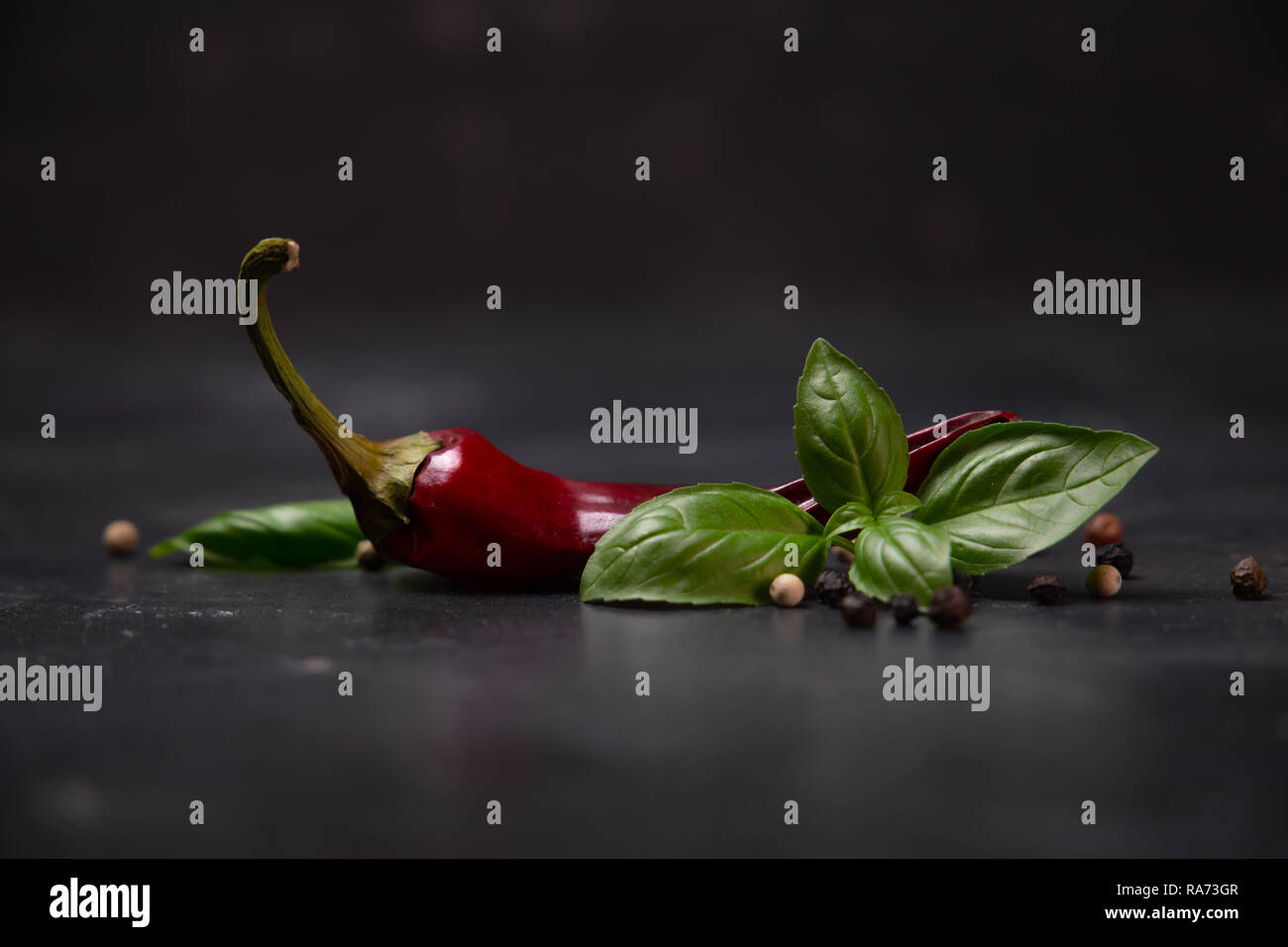 chili peppers with basil and peppercorns on a rustic surface Stock ...