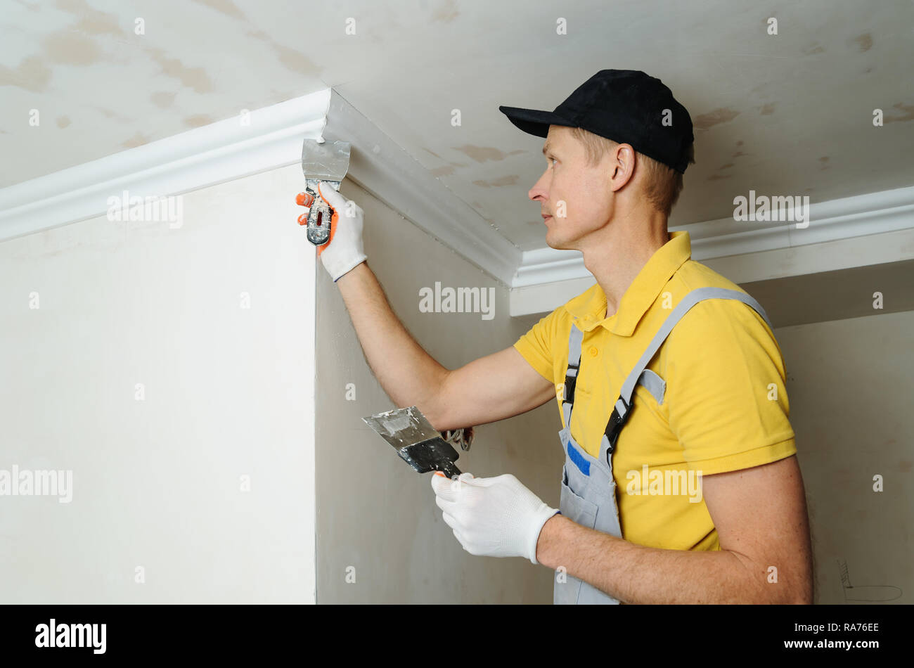 Installation of ceiling moldings. Worker puts glue on plastic molding ...