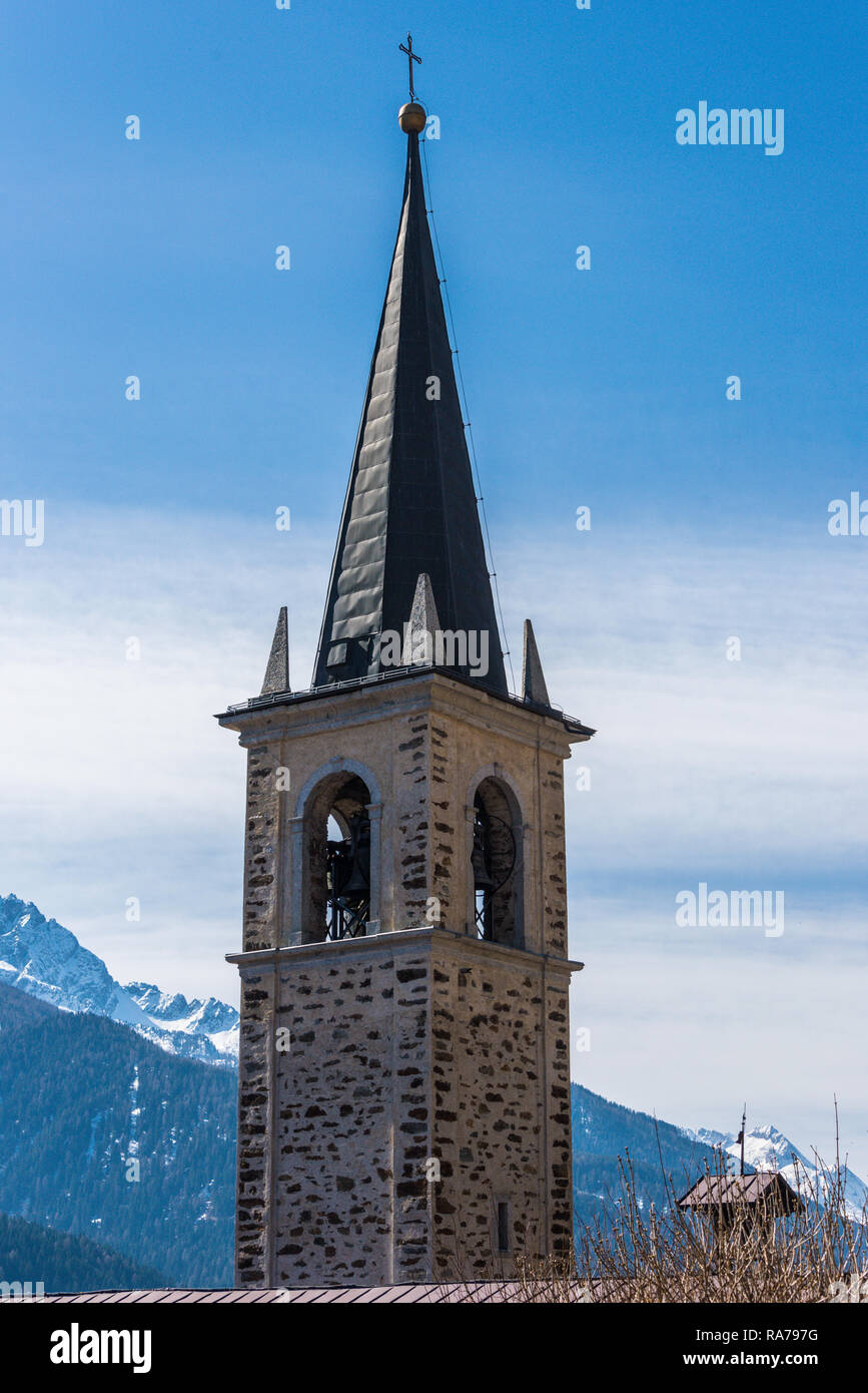 High, stone church bell tower against the blue sky and the snowy Alps ...