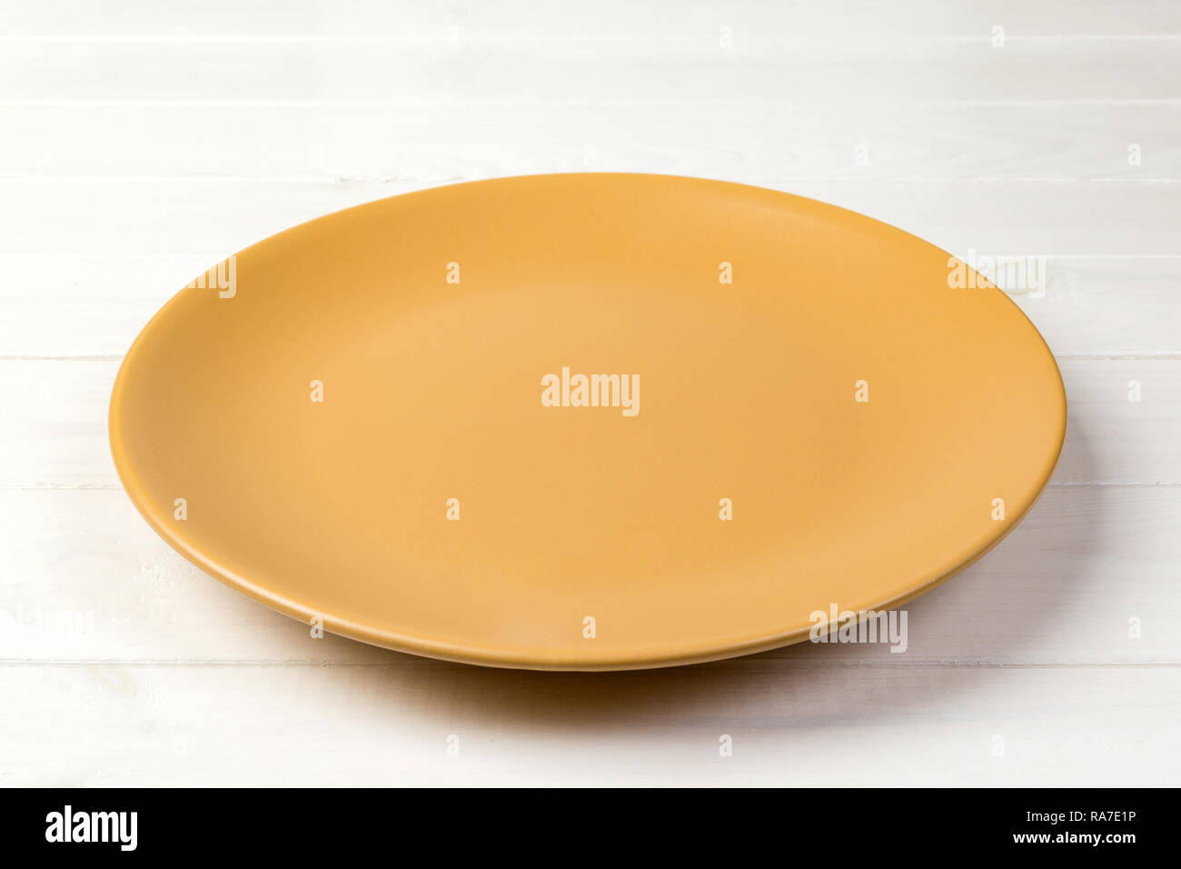 Perspective view. Empty yellow matte plate on white wooden background ...