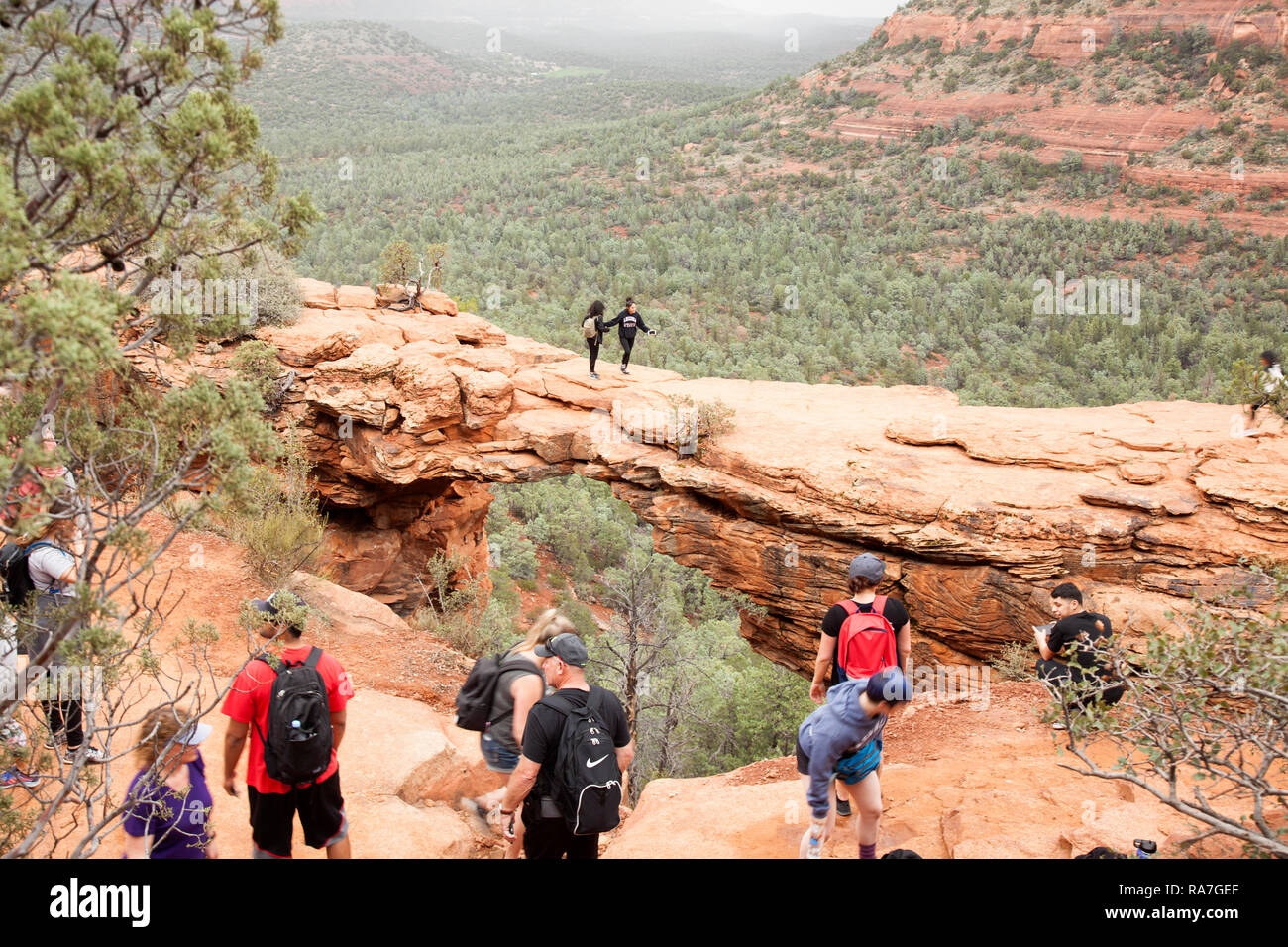 people walking along a natural stone arch calledDevils Bridge in Sedona ...