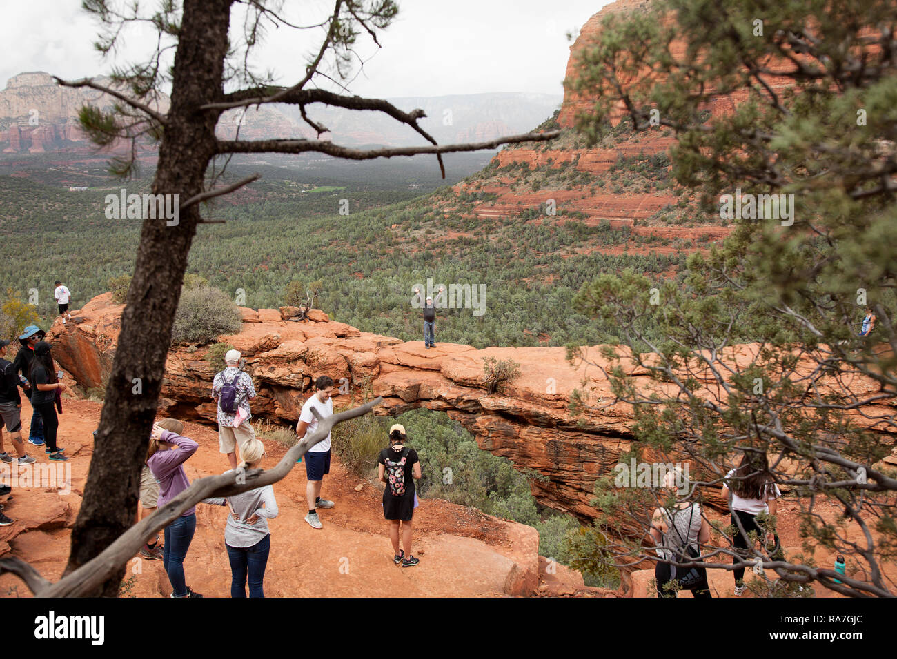 man walking along a natural stone arch called Devils Bridge in Sedona ...