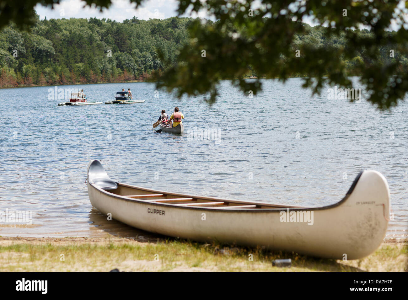 An empty canoe sits on the water near the beach of a lake during summer ...