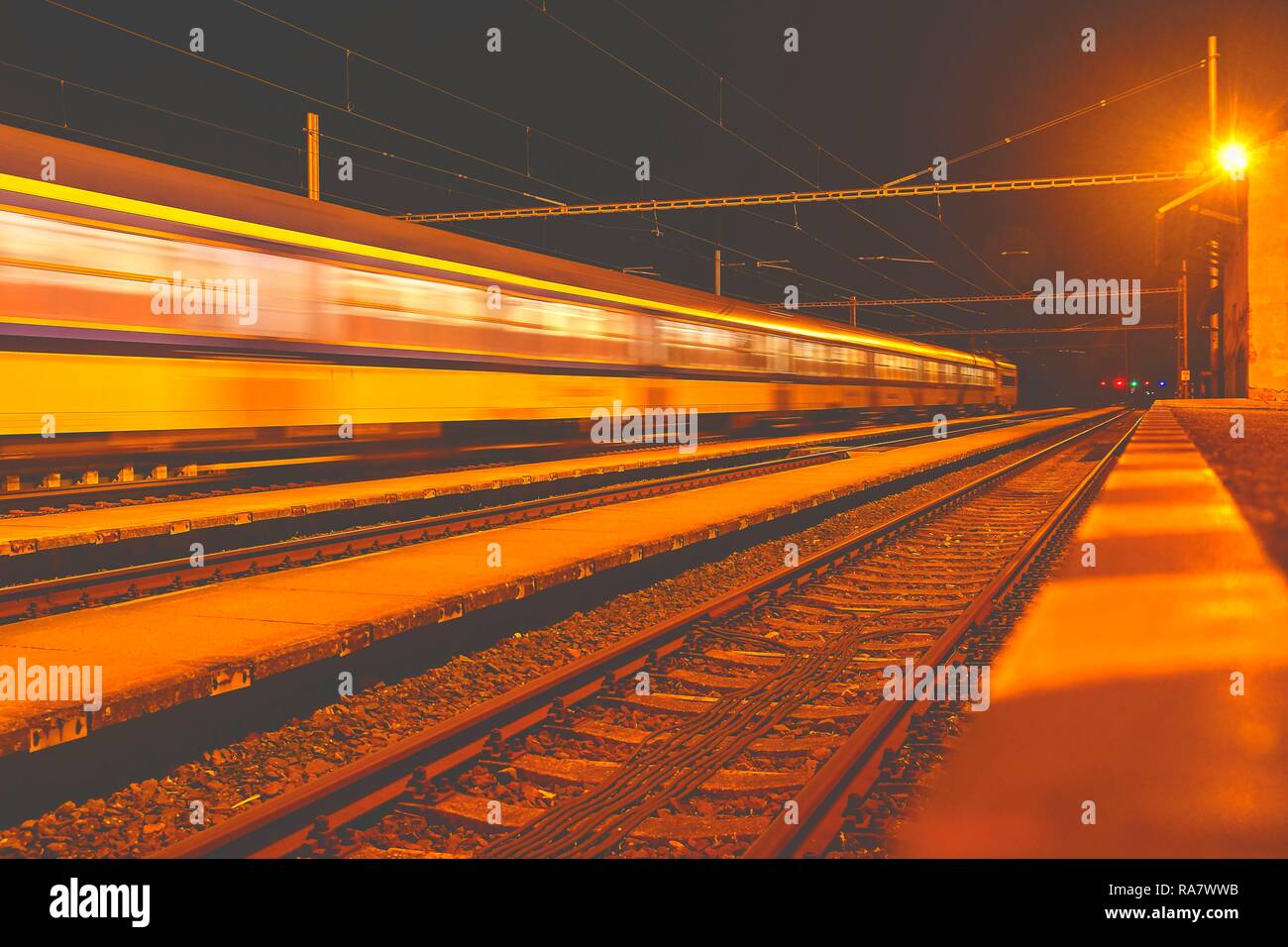 White and blue train passing a small roofless train station at night in ...
