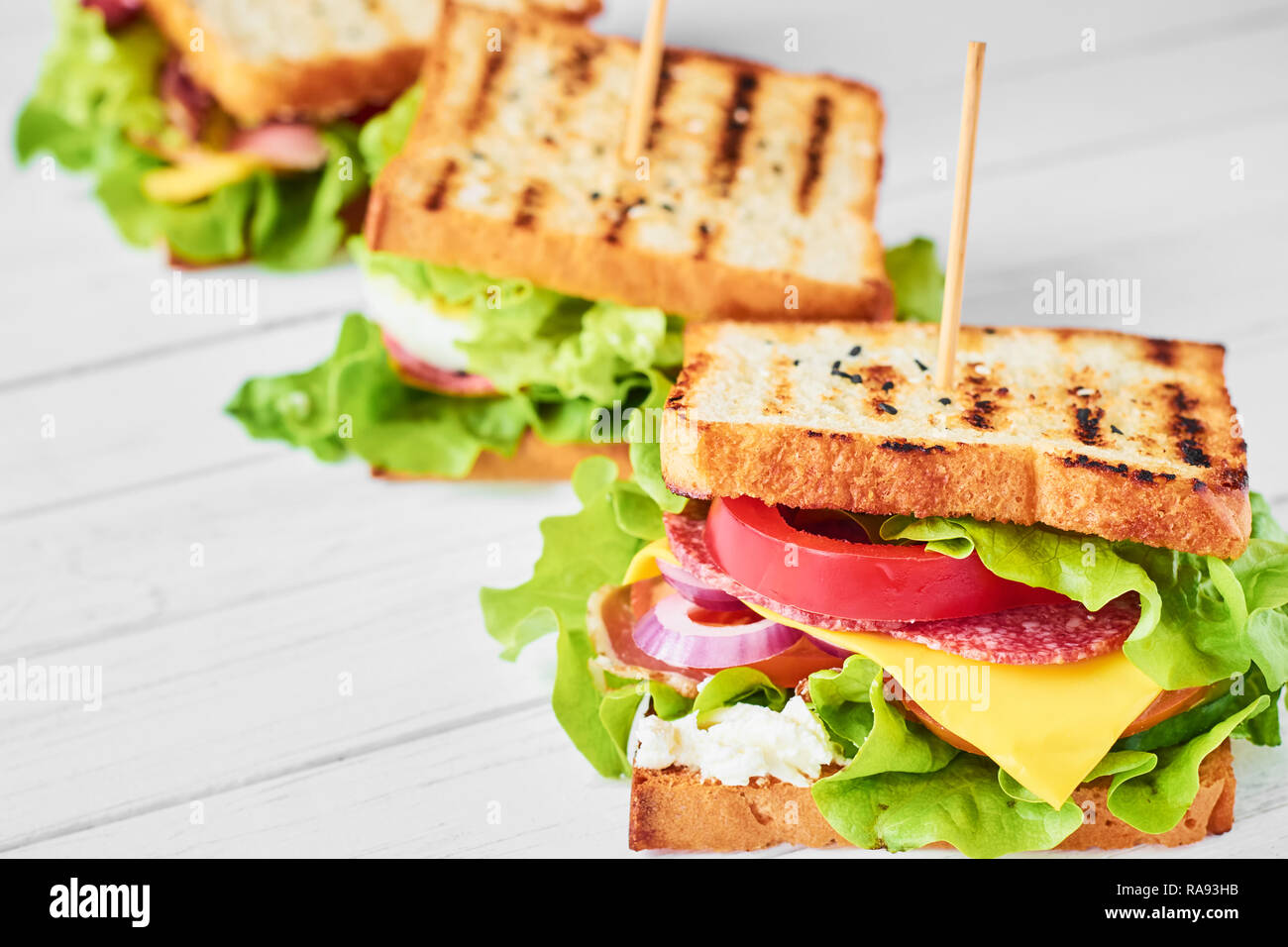 Three sandwiches with ham, lettuce and fresh vegetables on white ...