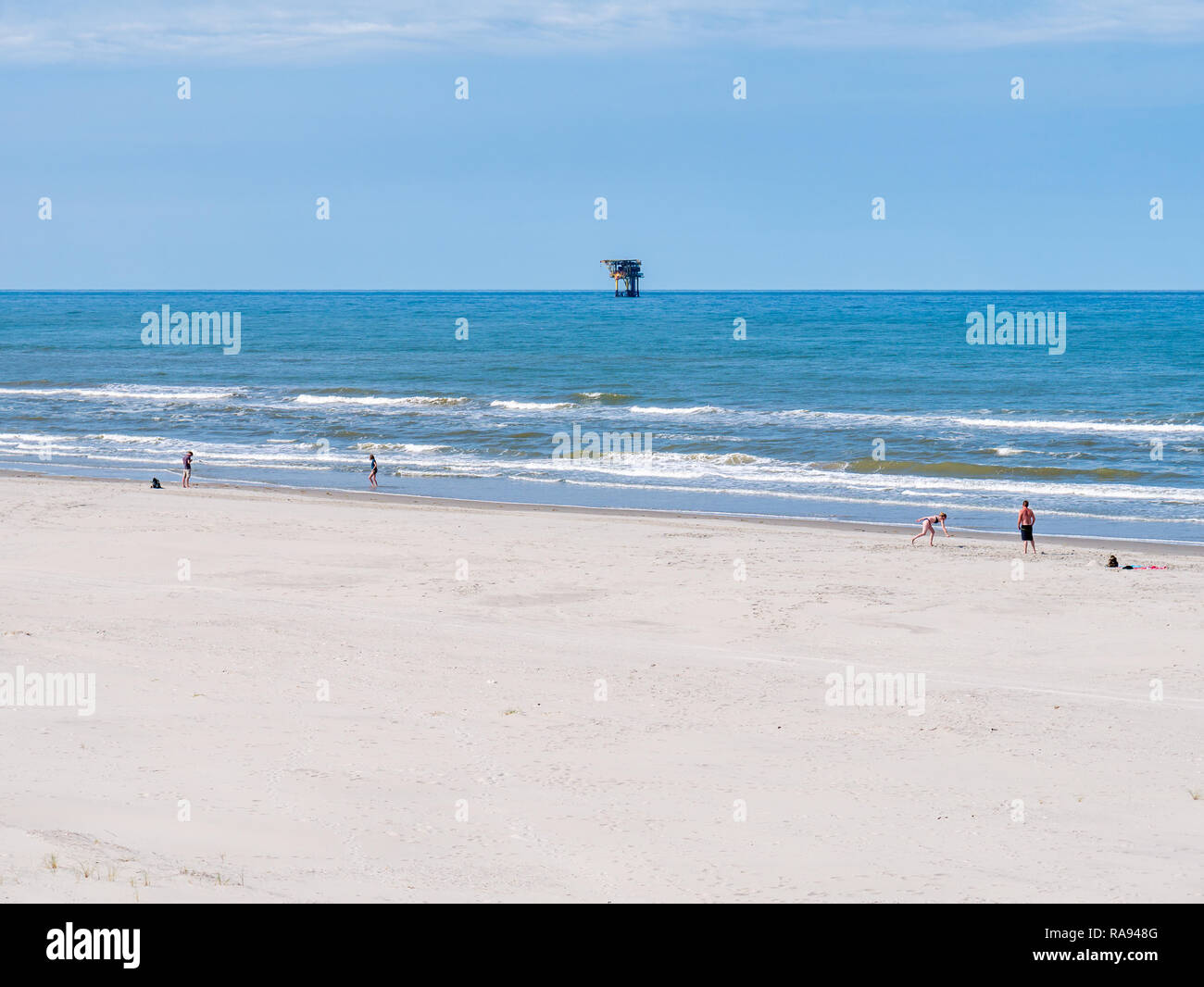 People playing on beach and North Sea with offshore drilling platform ...