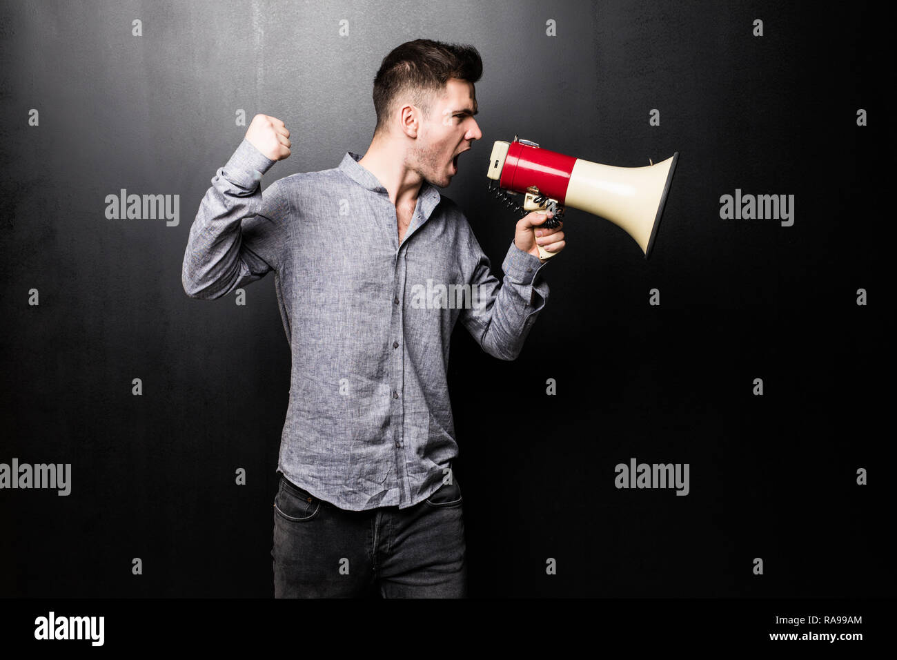 Portrait of young man yelling into the megaphone over black background ...