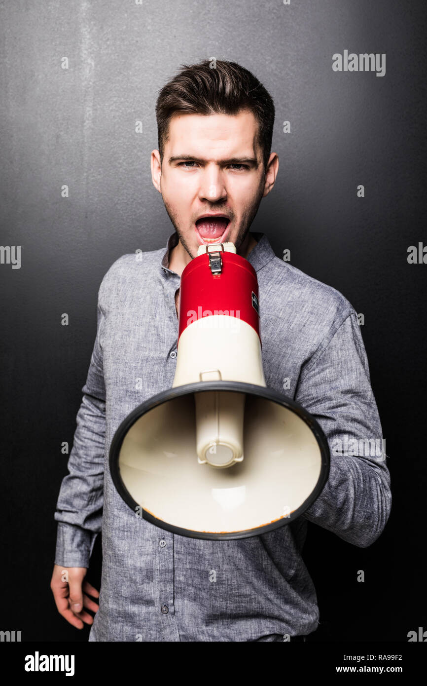 Portrait of young man yelling into the megaphone over black background ...