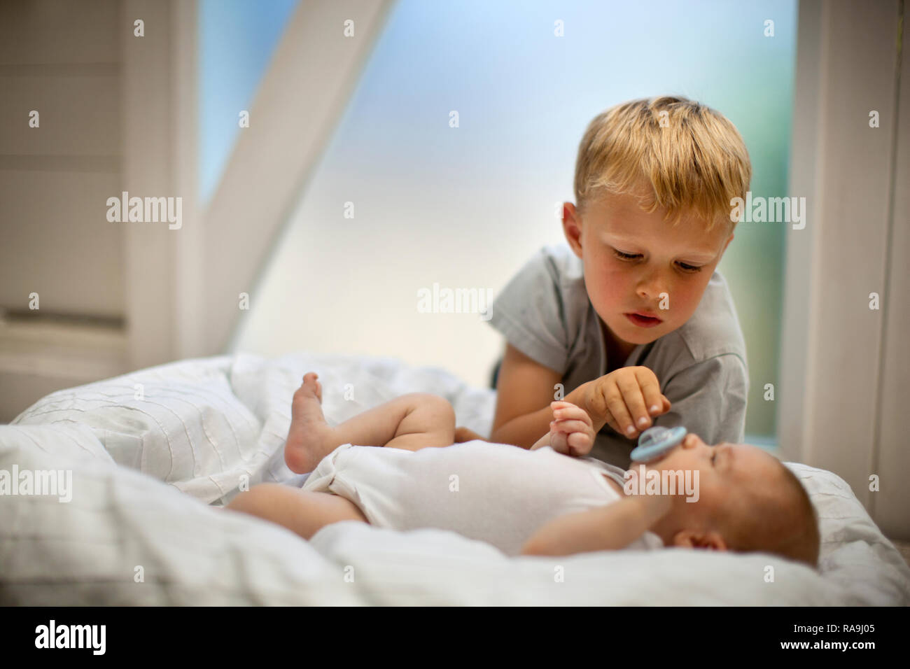 Young Boy looking over baby boy holding his dummy in Stock Photo - Alamy
