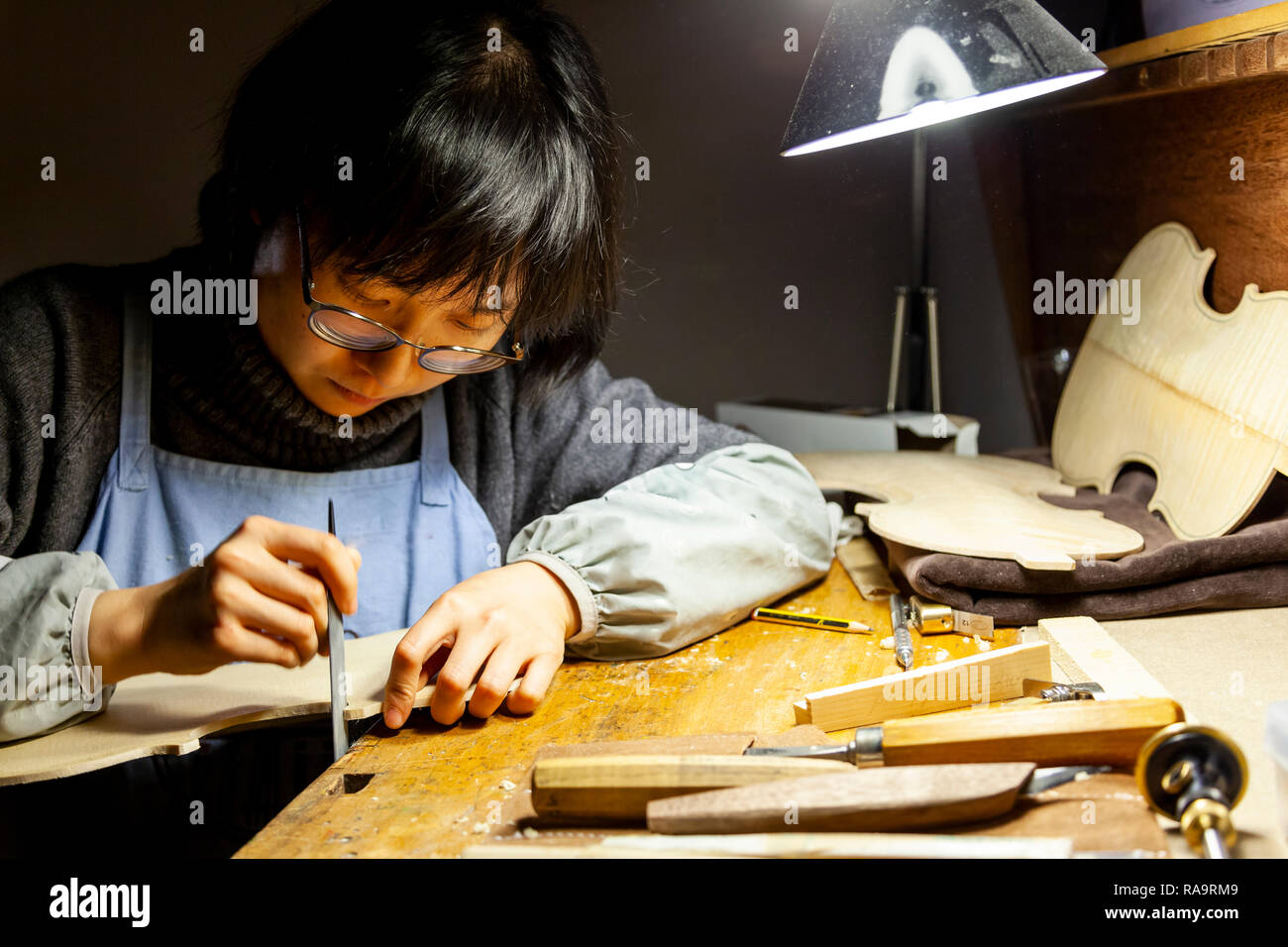 female craftsman violin maker working on a new violin in the workshop ...