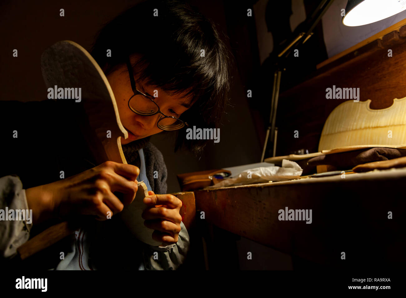 female craftsman violin maker working on a new violin in the workshop ...