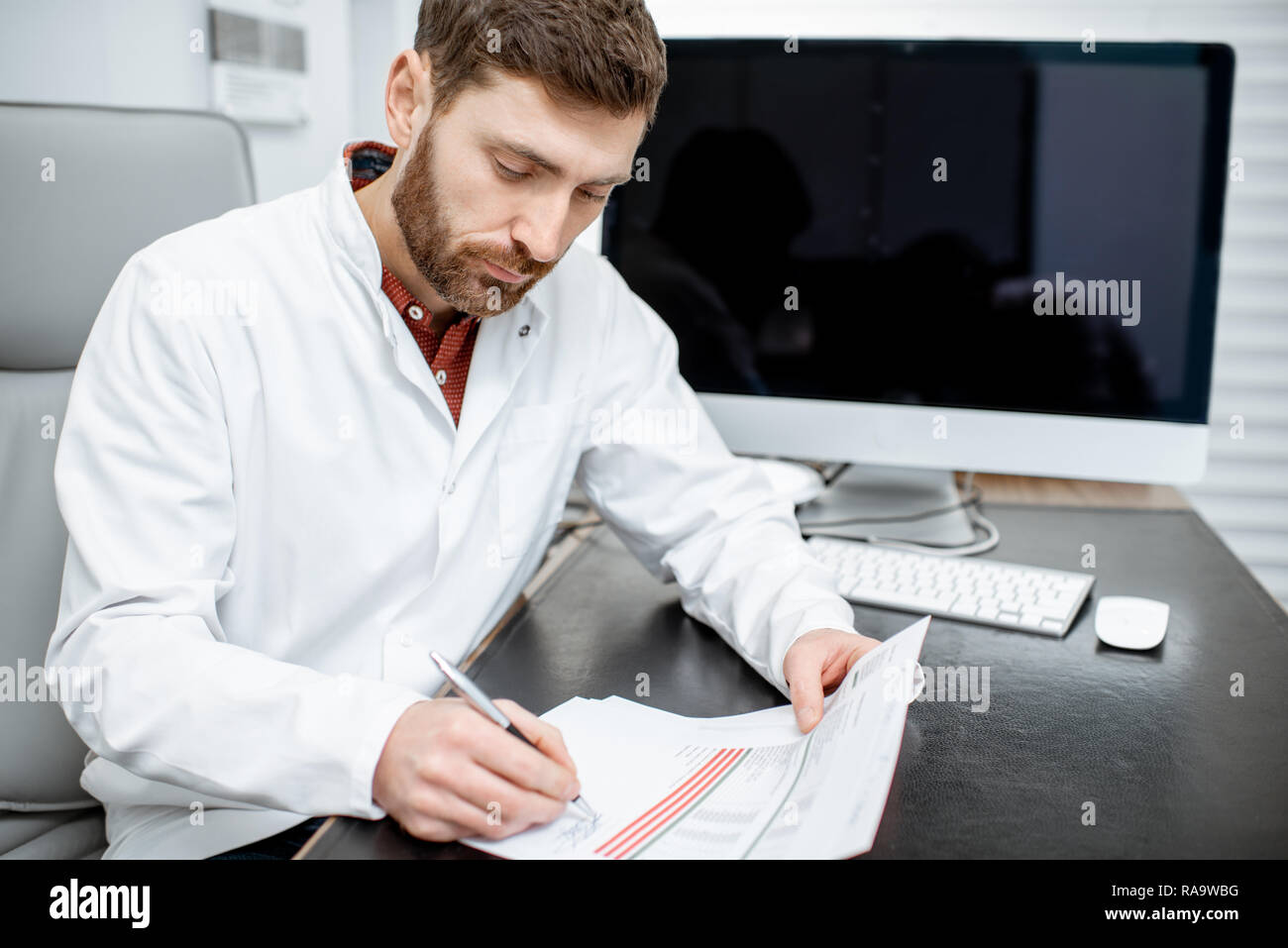 Handsome doctor signing some documents sitting in his luxury medical ...