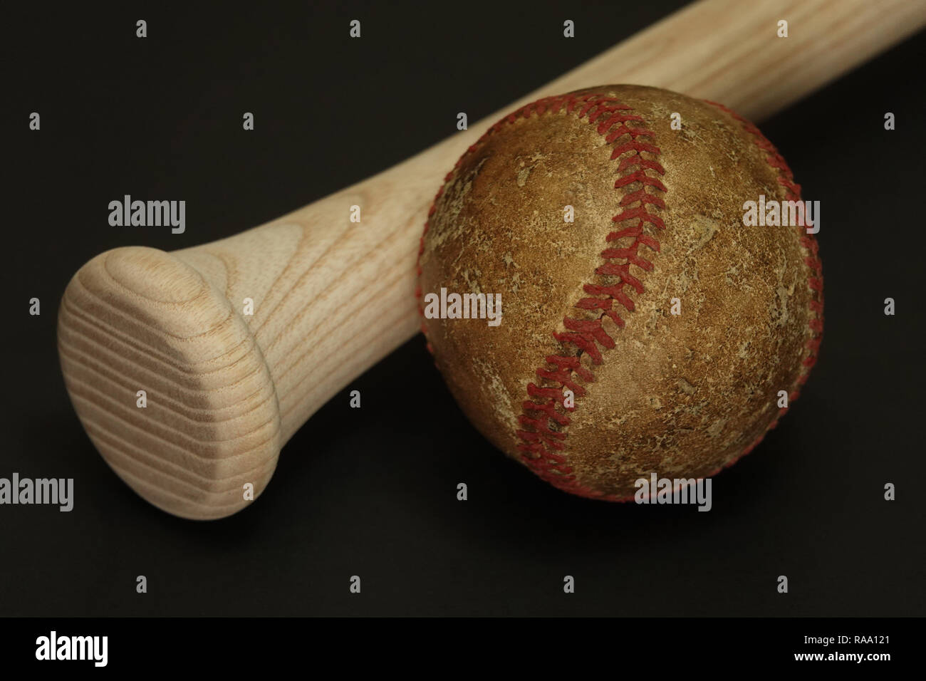 An old and well used baseball is shown next to a new, wood baseball bat ...