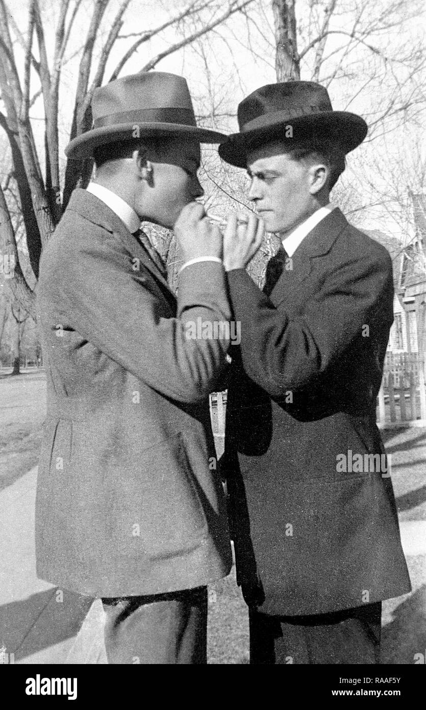 Two dapper men get close and light each others cigarettes, ca. 1930 ...