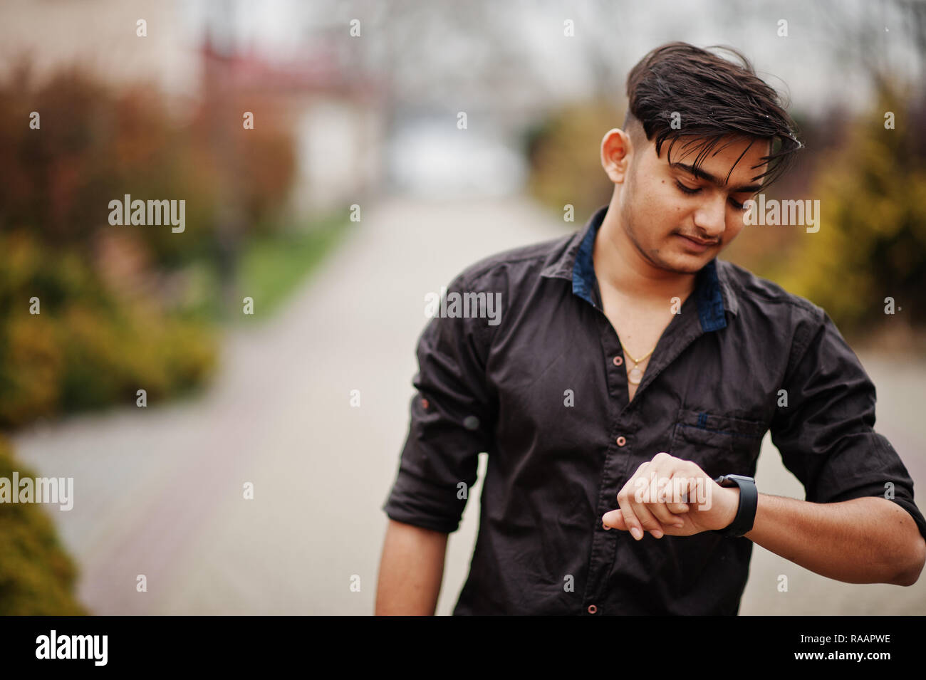 Indian man in brown shirt posed outdoor and looking at his watches ...