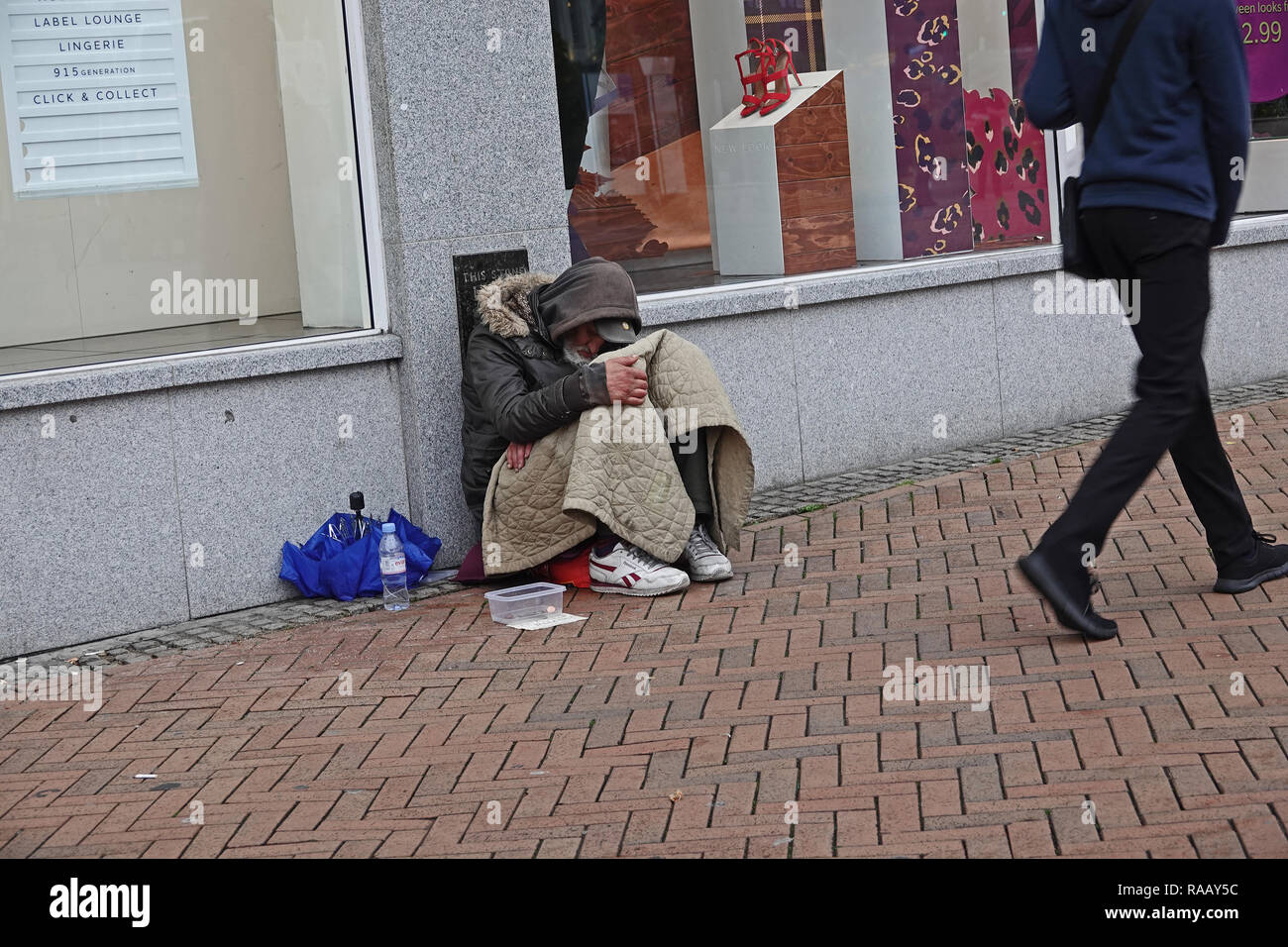 Homeless man begs outside a shop as public passes by Stock Photo - Alamy
