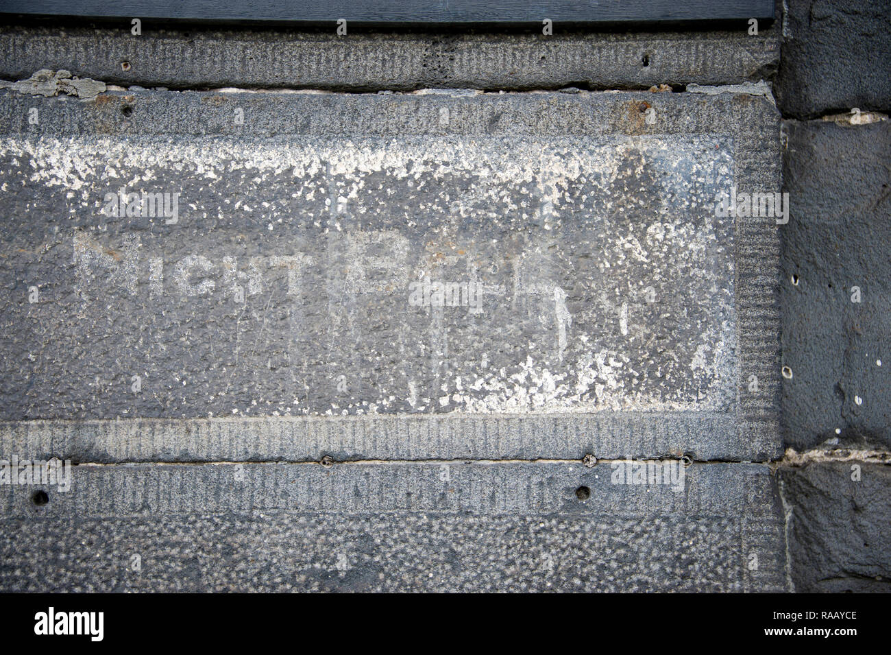 A faded and partially worn painted sign on a stone fence reading Night ...