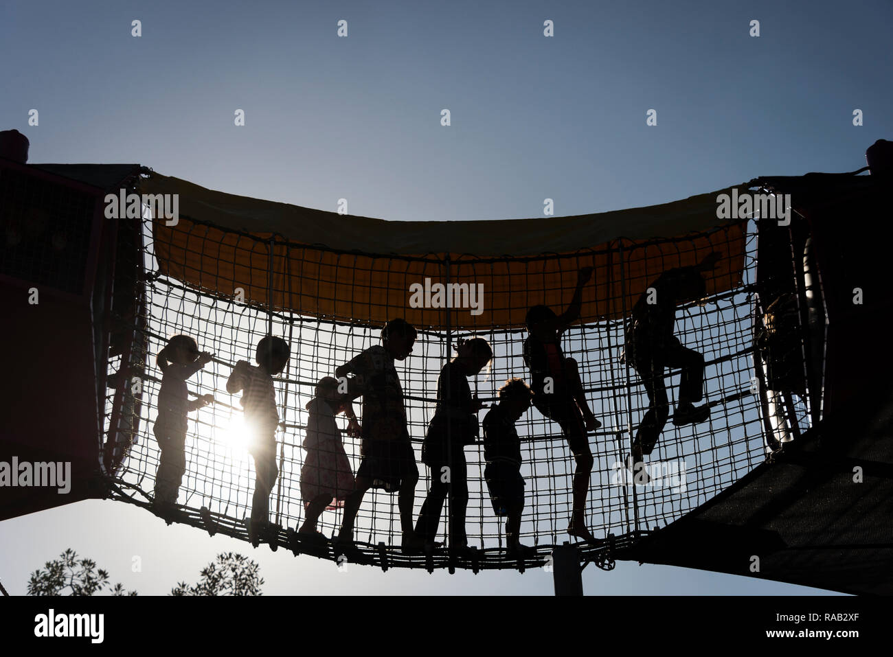 Children, in silhouette, crossing a playground net bridge Stock Photo ...