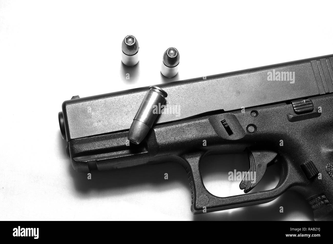 A black semi automatic 9mm pistol on a white background with three hollow point bullets shown in ...