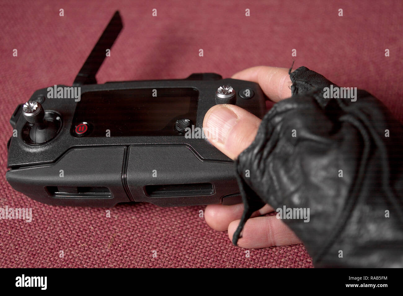 A hand wearing leather glove holding abstract remote control, on red ...