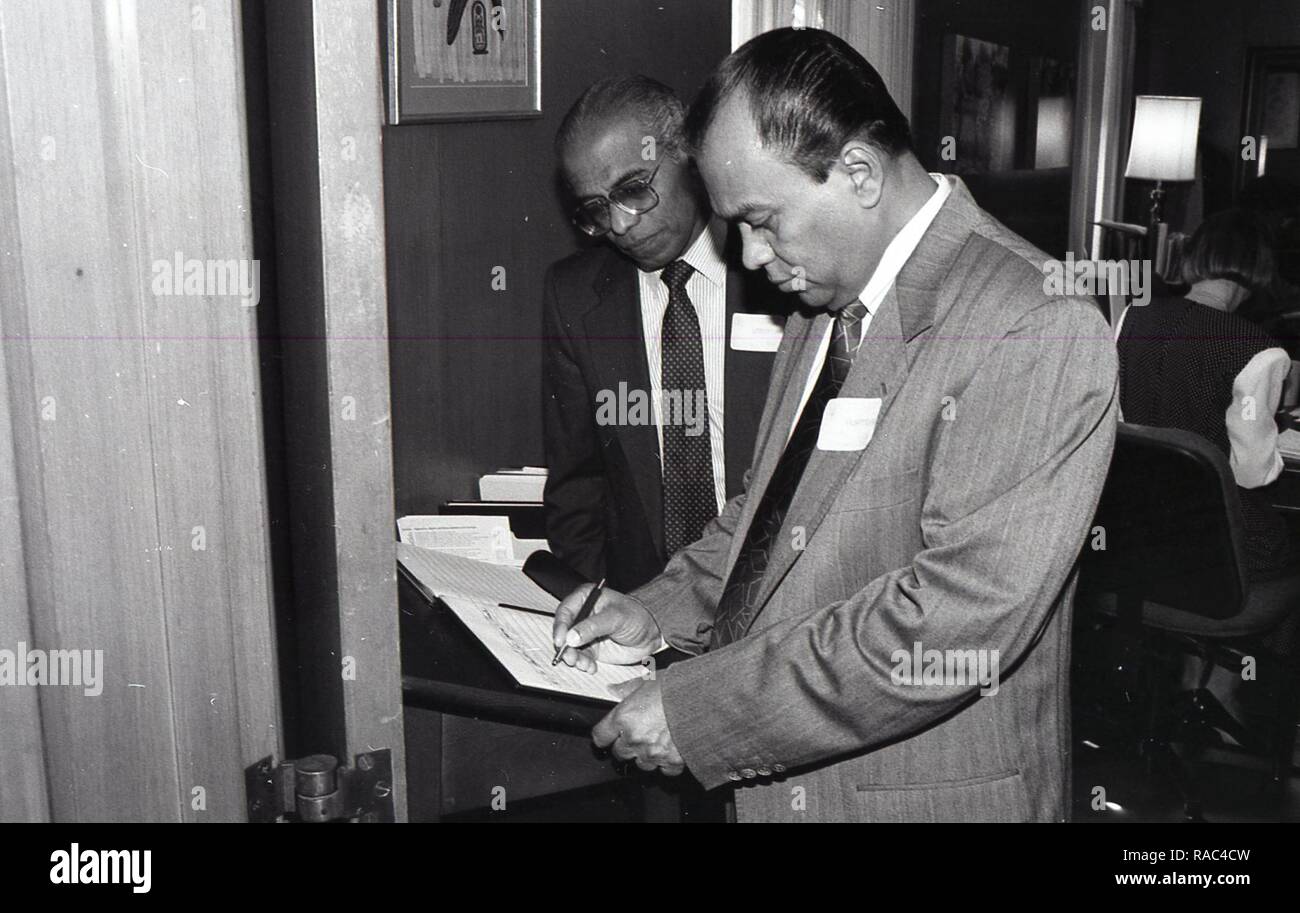 A MAN SIGNING THE BOOK WITH ANOTHER MAN LOOKING Stock Photo - Alamy