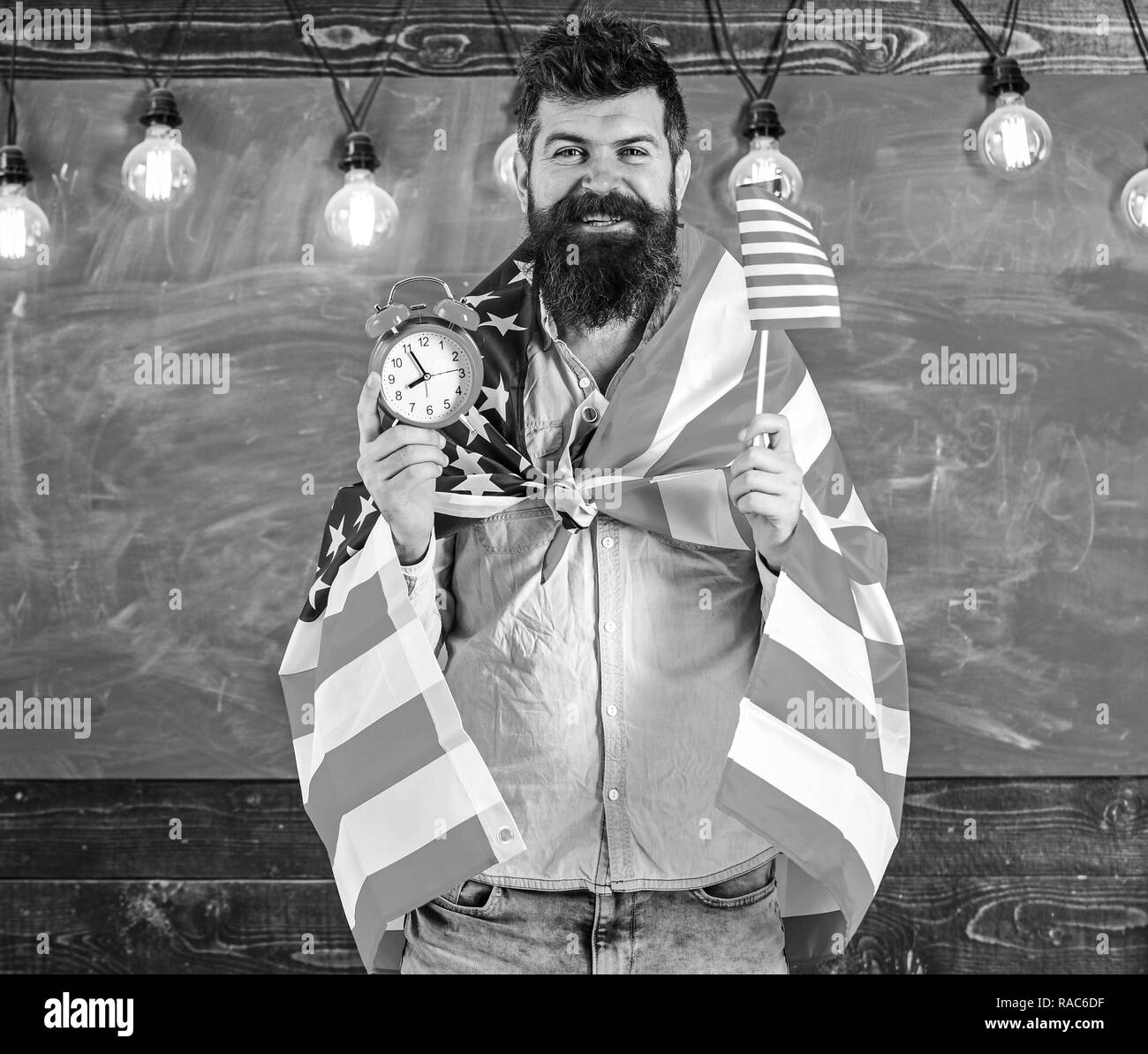 Man with beard on happy face holds flag of USA and clock in classroom ...