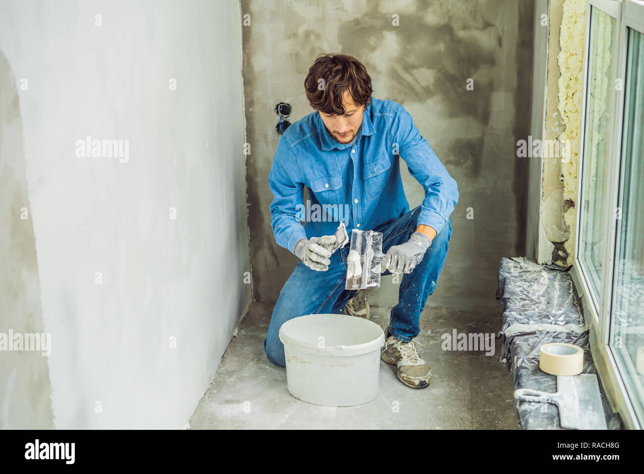 master is applying white putty on a wall and smearing by putty knife in ...