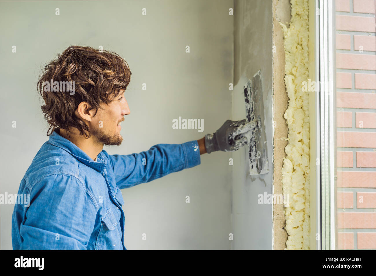 master is applying white putty on a wall and smearing by putty knife in ...