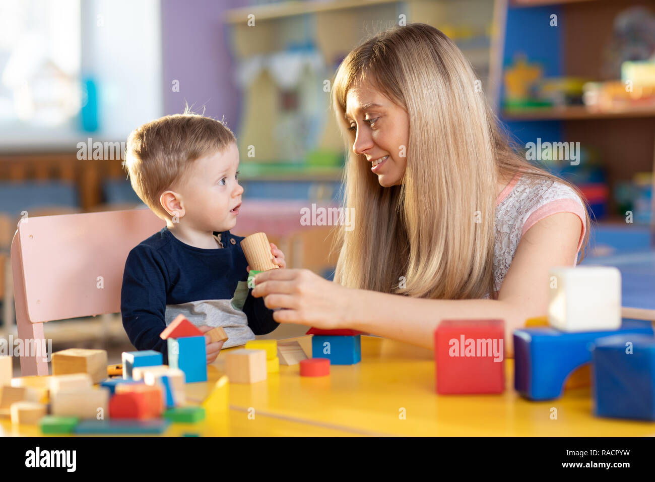 Cute kindergarten teacher and baby toddler playing educational toys at ...