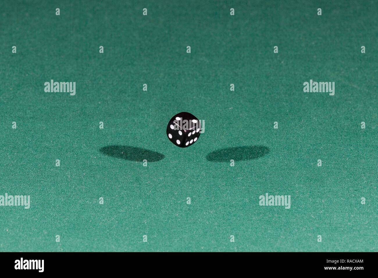 One black dice falling on a green table Stock Photo - Alamy