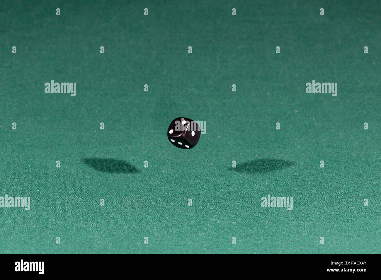 One black dice falling on a green table Stock Photo - Alamy