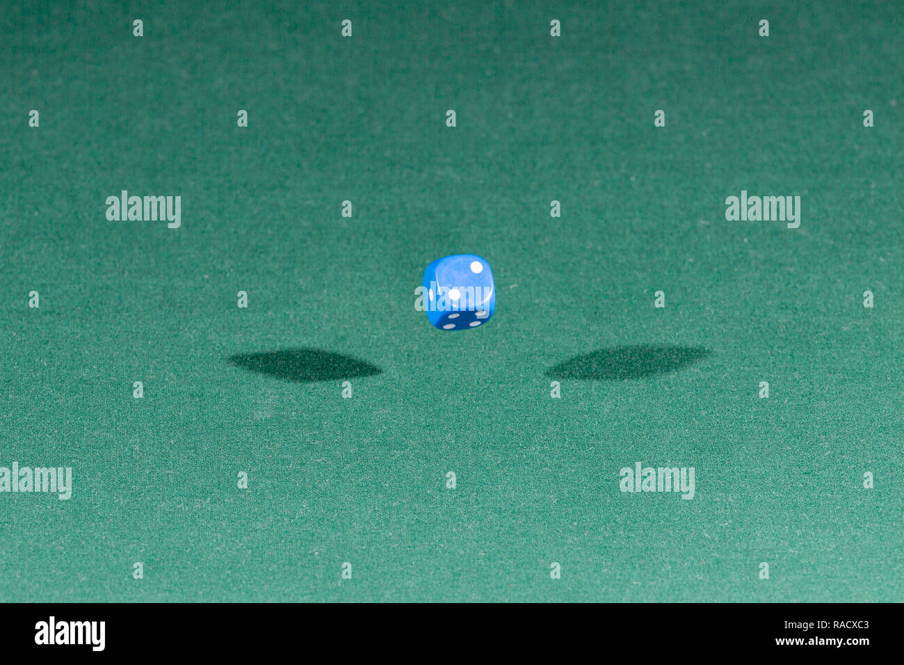 One blue dice falling on a green table Stock Photo - Alamy