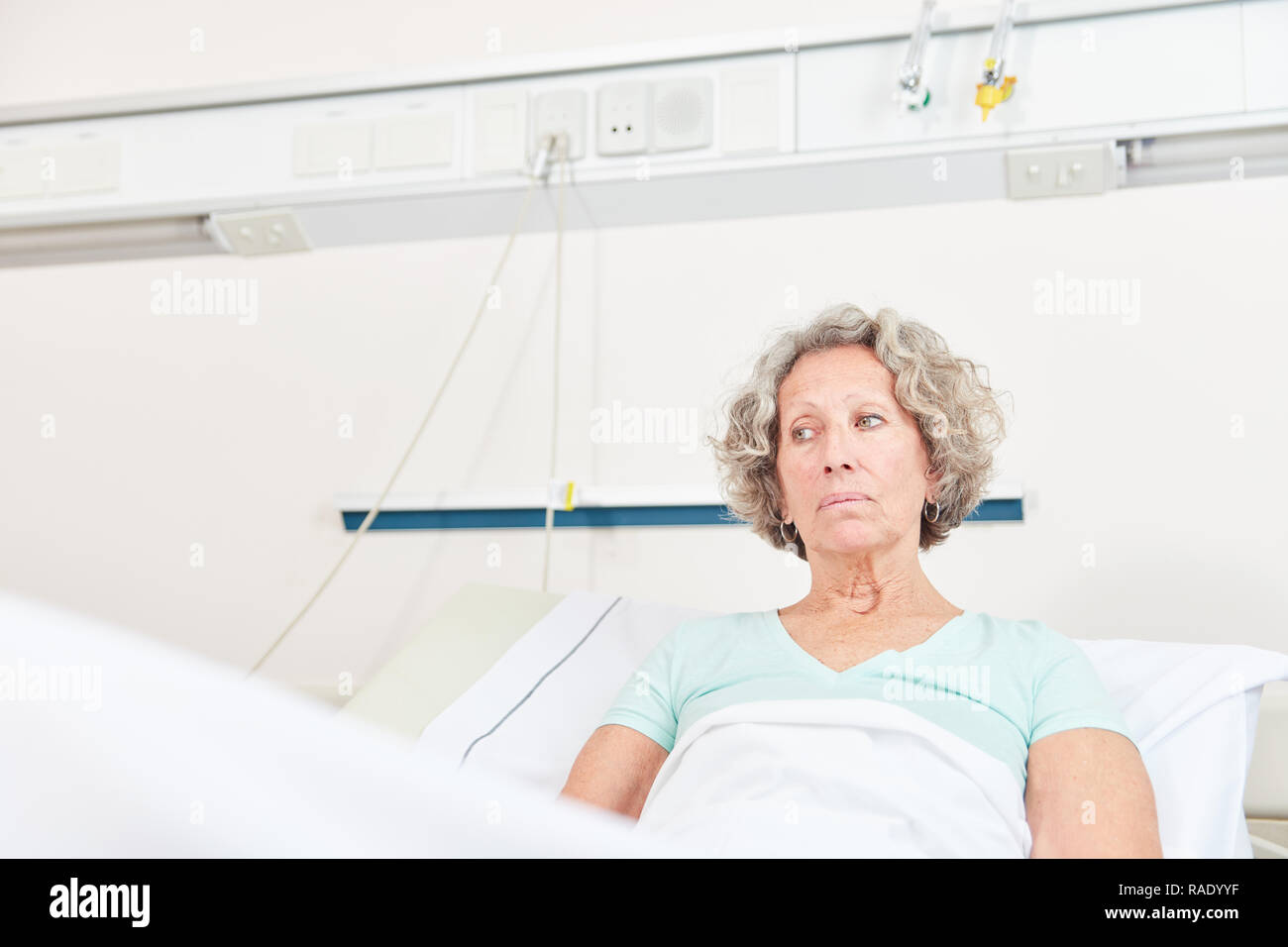 Woman as an unhappy patient lies in the hospital bed and looks worried ...