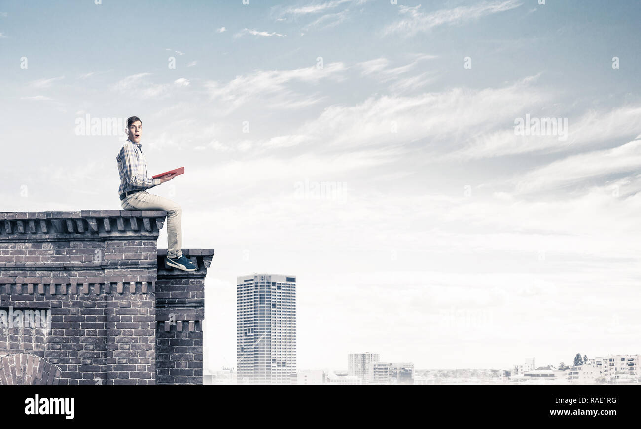 Man on roof edge reading book and cityscape at background Stock Photo ...