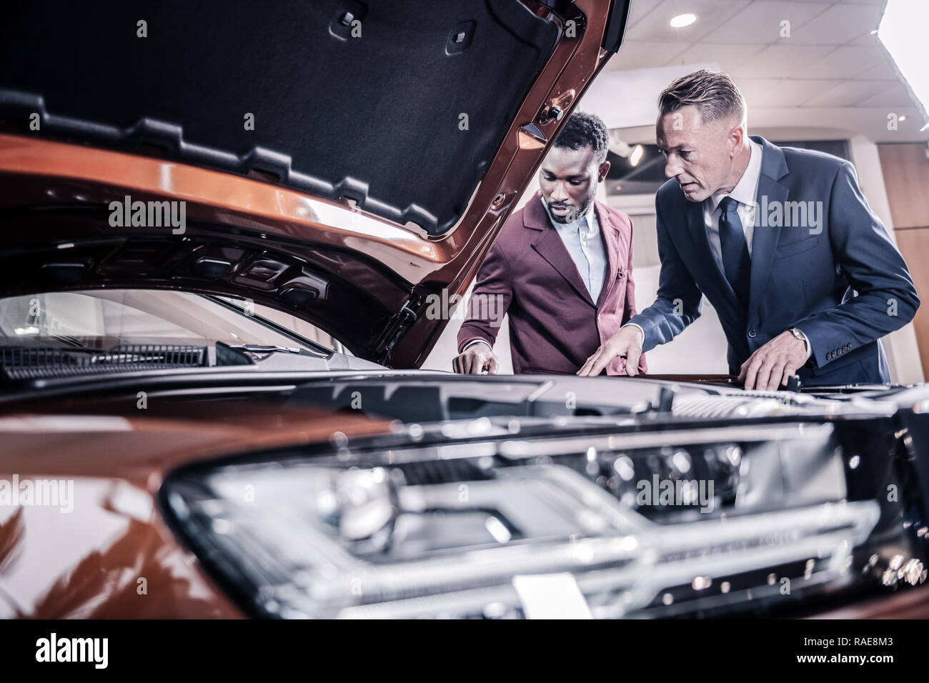 Two men standing near brown hatchback car with opened front trunk Stock ...