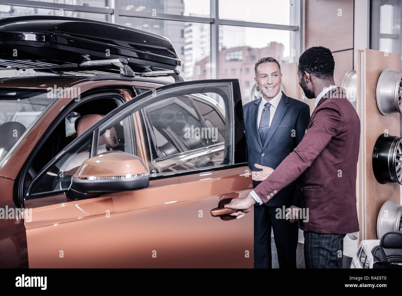 Sales manager wearing dark red jacket opening door of car for his ...
